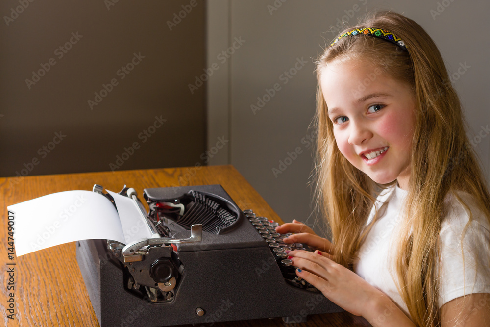 Pretty blonde little girl typing a letter on a vintage black typewriter ...