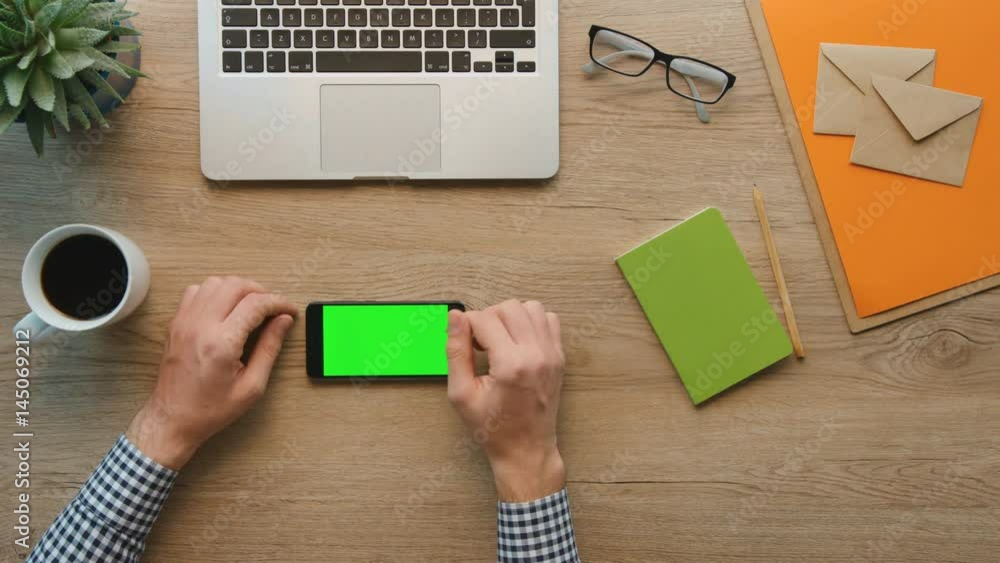 Man using horizontal smart phone with green screen on wooden table ...