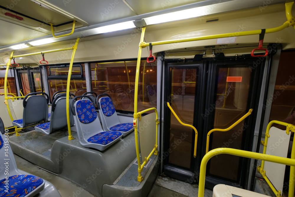 Interior of modern city bus with seats, doors and handles in night ...