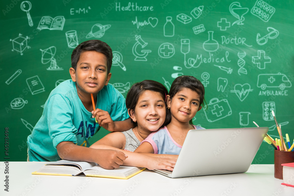 indian school kids using laptop in a classroom over green chalkboard ...