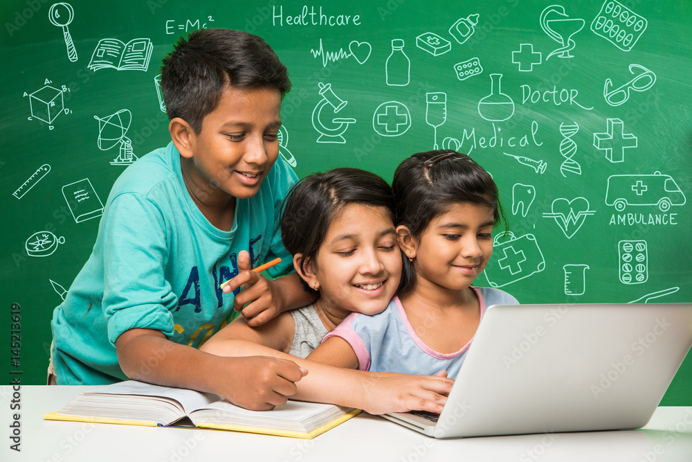 indian school kids using laptop in a classroom over green chalkboard ...
