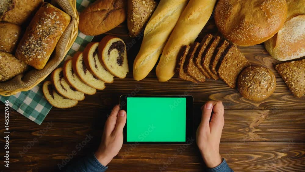Man using tablet device with green screen on wooden table with fresh ...