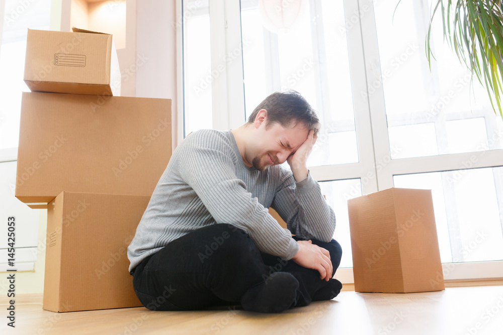 Worried and frustrated young man sitting on packaged boxes at house for ...