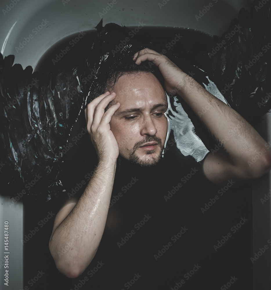 Fallen angel, man in a bathtub with black water and wings, submerged ...