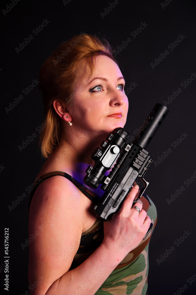 A middle aged, white, woman holds a semi automatic pistol with silencer and collimator against ...