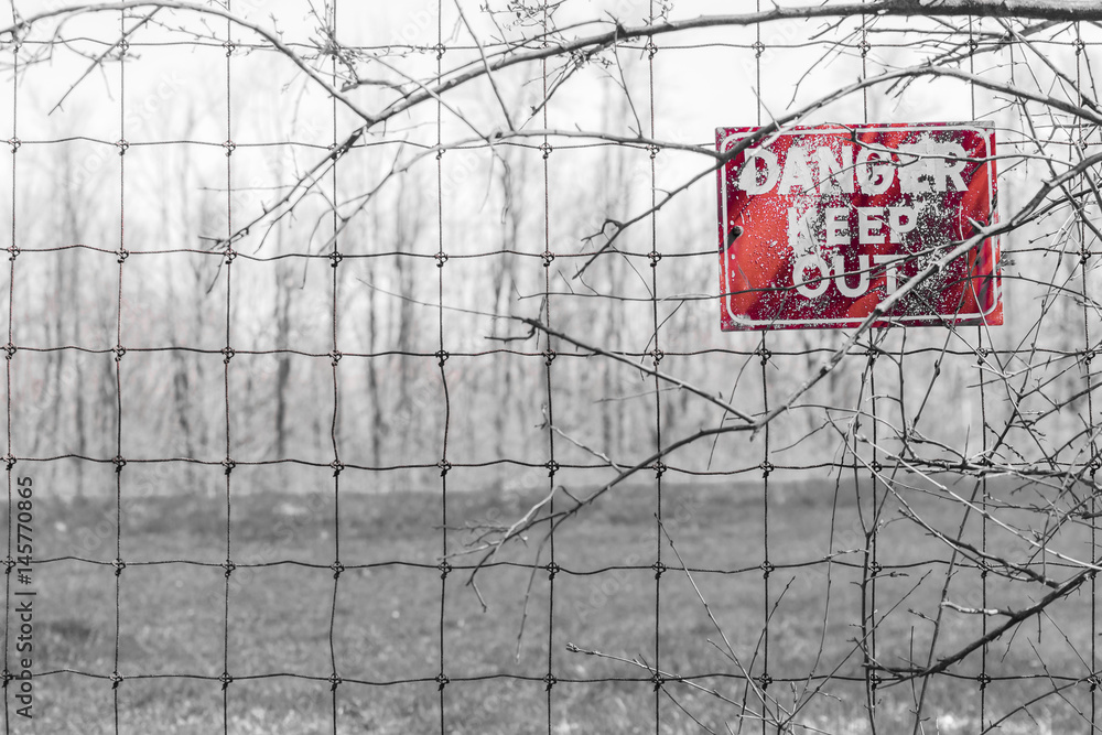 Red Danger sign posted to barbed fence tangled in branches, warning ...