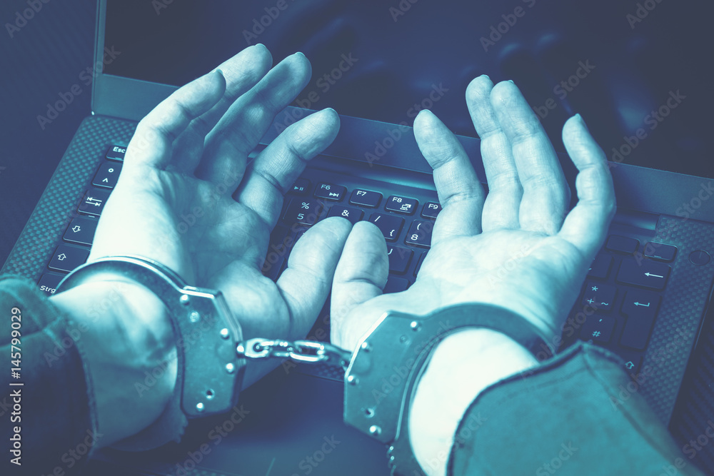 Blue matt toning image of arrested hacker with hands in handcuffs on ...