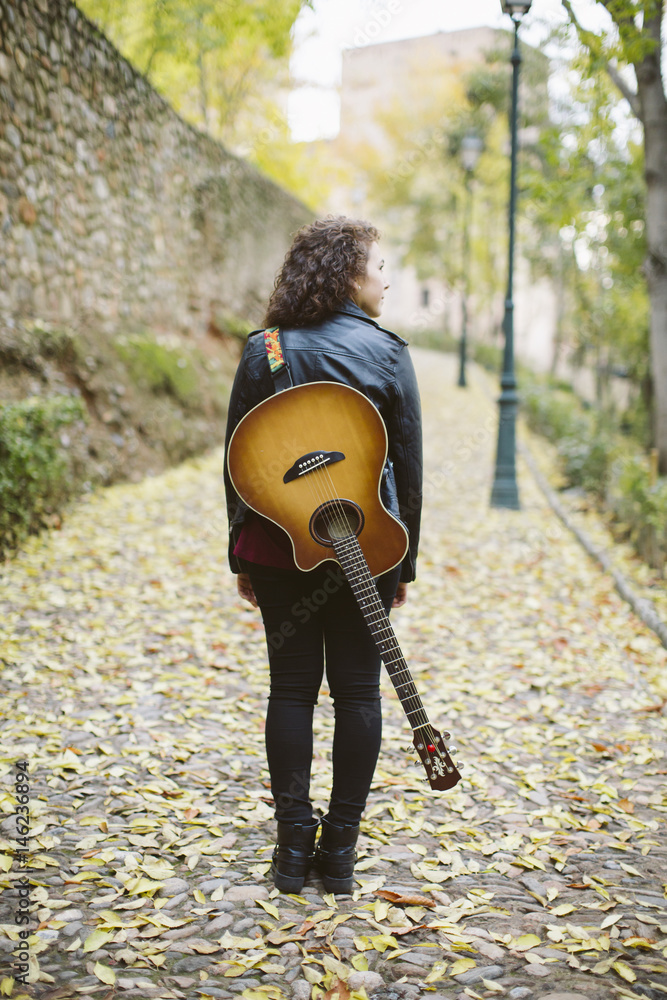 Beautiful young woman standing backwards with her guitar. Girl wearing ...