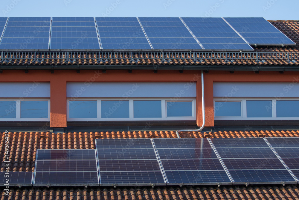 Solar panel on a red roof reflecting the sun and the cloudless blue sky ...