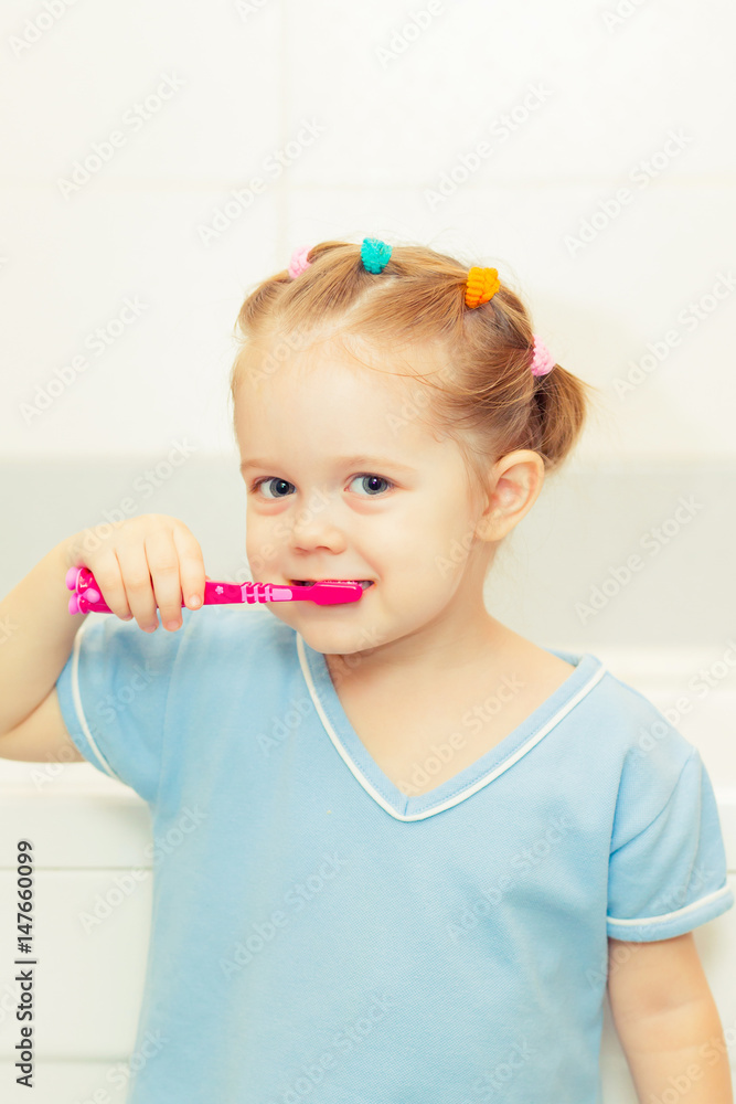 Little girl brushing her teeth in the bathroom. Smiling child holding a ...