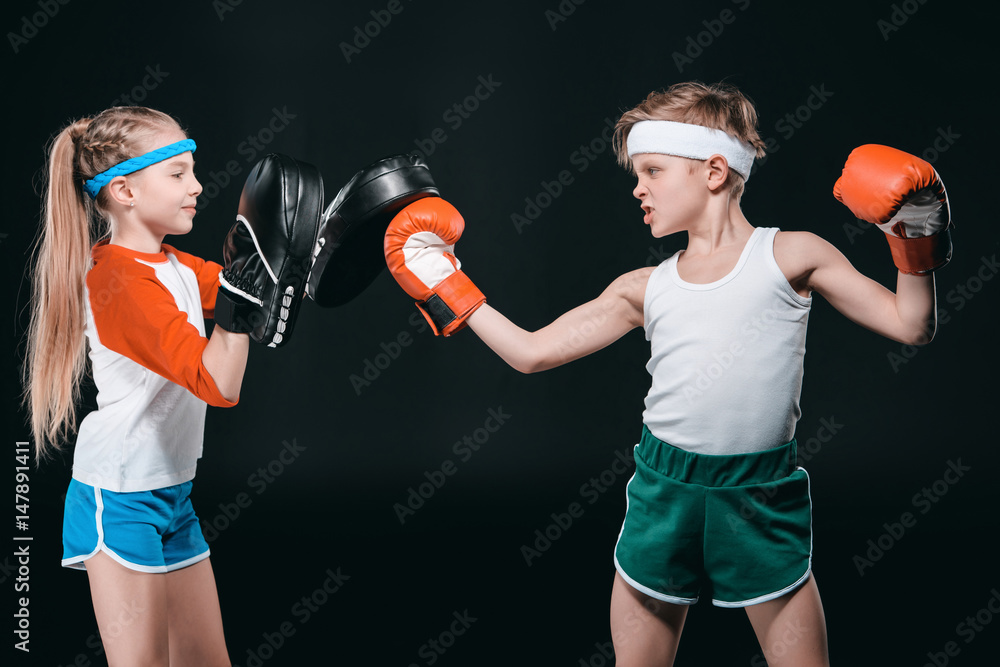 Side view of boy and girl in sportswear boxing isolated on black ...