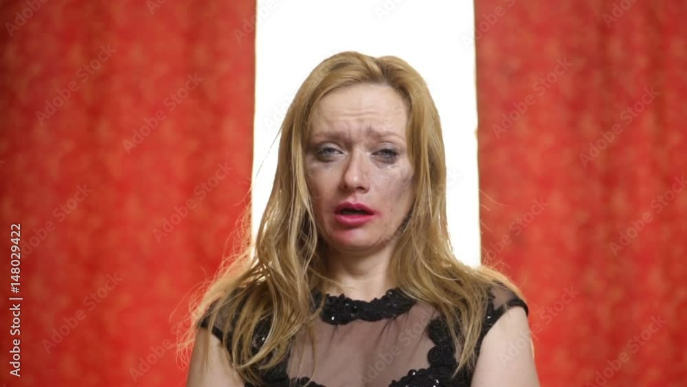 Beautiful sad woman with red lipstick and makeup cries on a red against ...