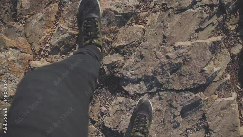 Feet over the abyss. Only legs: the tourist sits on the edge of the ...