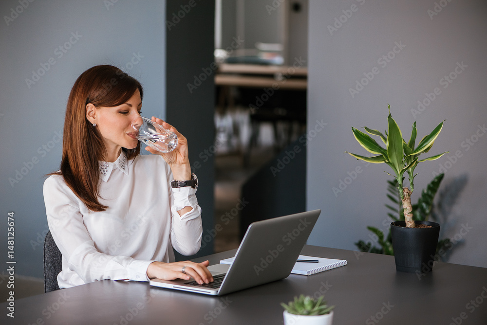 Stay hydrated. Pretty young woman in the office drinking water while ...