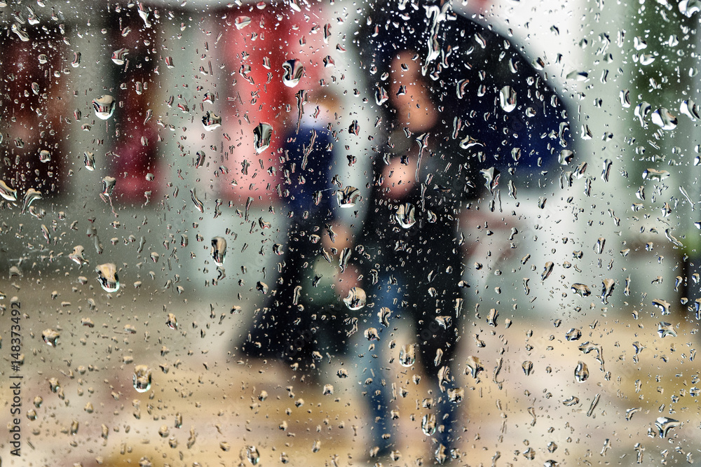View through sharp raindrops on the window glass at the girl in a black ...