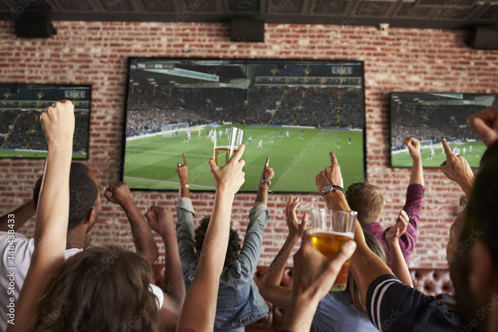 Foto de Rear View Of Friends Watching Game In Sports Bar On Screens do ...