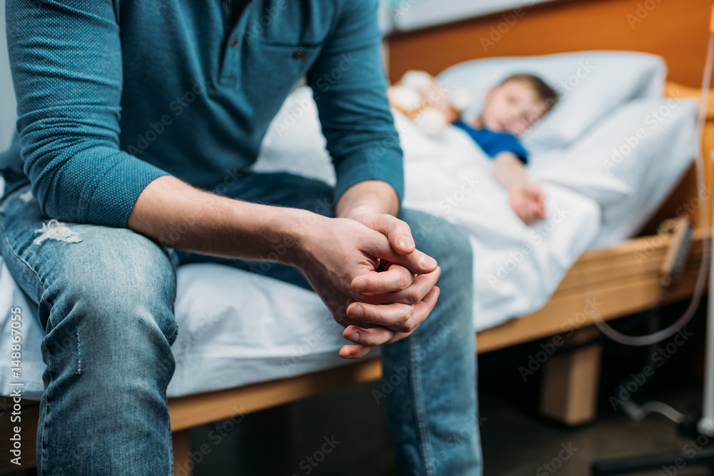 partial view of dad sitting near sick son in hospital bed Stock Photo ...