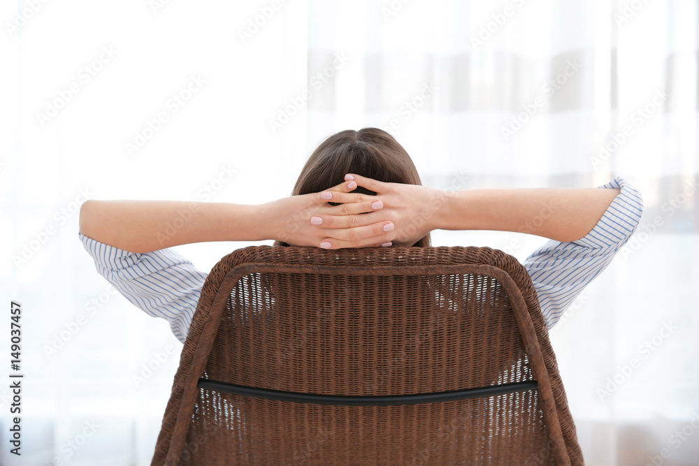 Rear view of relaxed woman with hands behind her head sitting on chair ...
