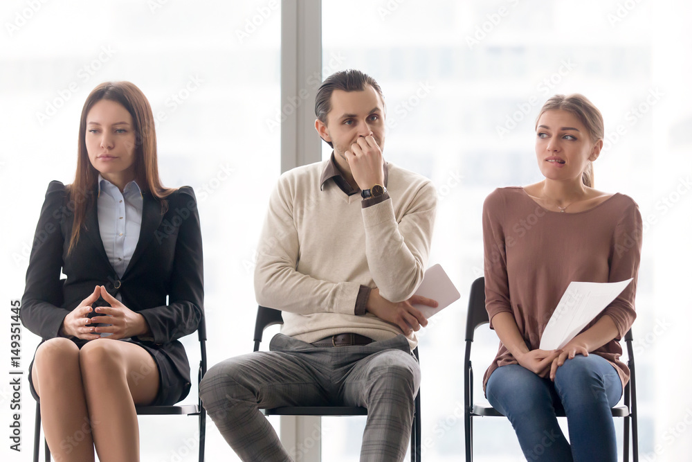 Man and two women sitting on chairs in row, expressing different ...