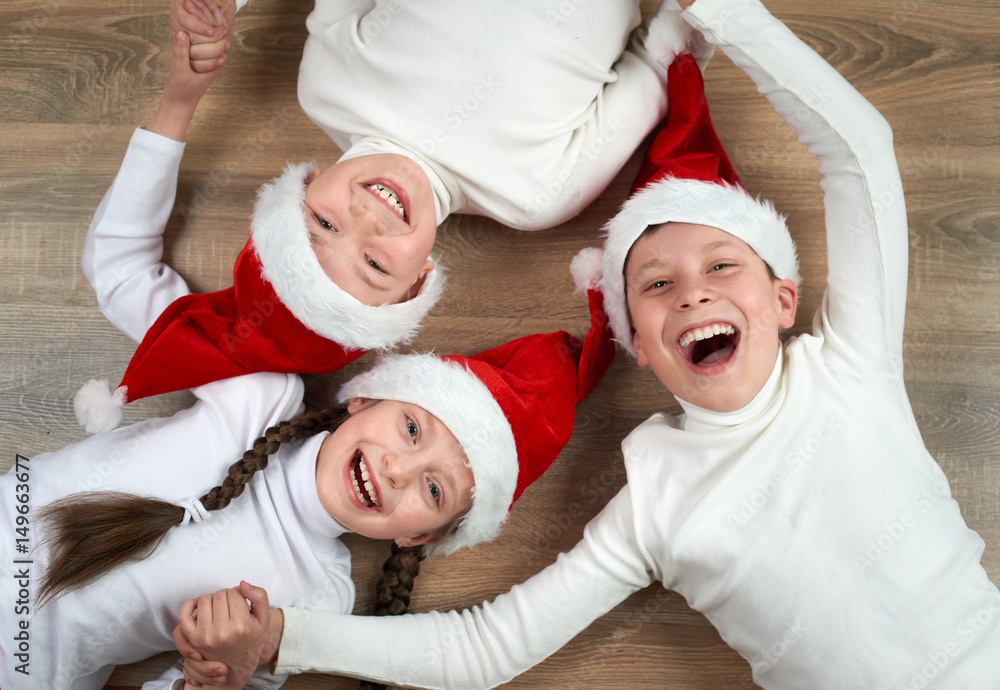 three kids in Santa hats lying on wooden background, having fun and ...