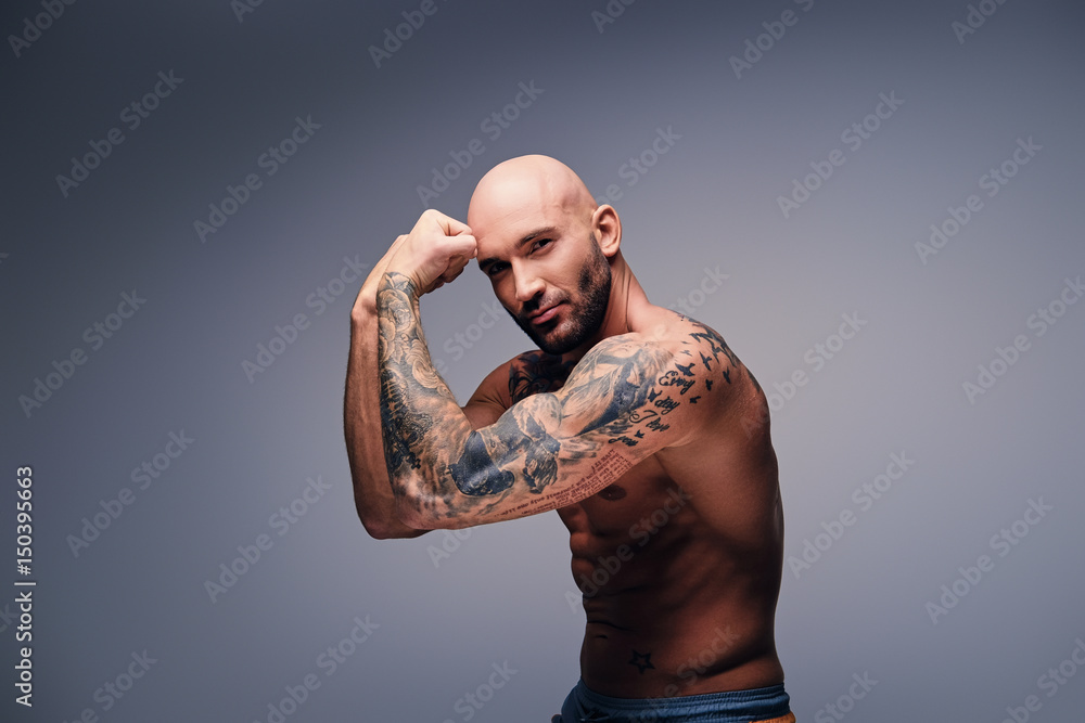 handsome muscular shaved head male with tattooed torso shows his ...