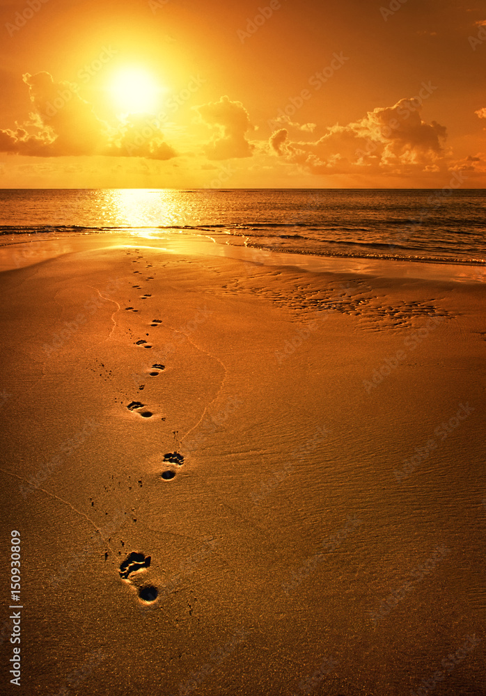 Single footsteps on beach walking towards sun of coastal horizon. Stock ...