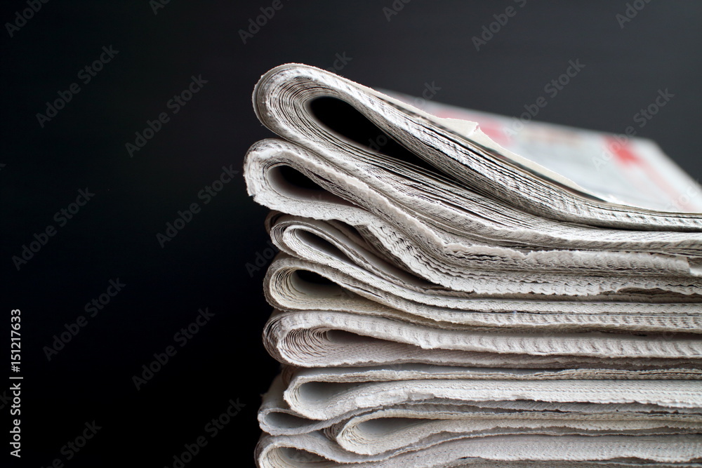 Stack of folded newspapers in front of a black background with copy ...