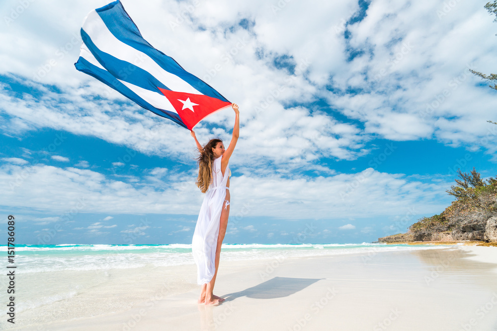 Beautiful young blond woman in white dress and bikini swimsuit stands a back holds the cuban ...