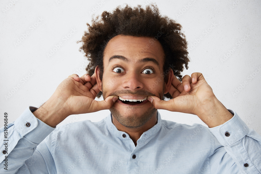 Funny goofy young dark-skinned man grimacing stretching mouth with both ...