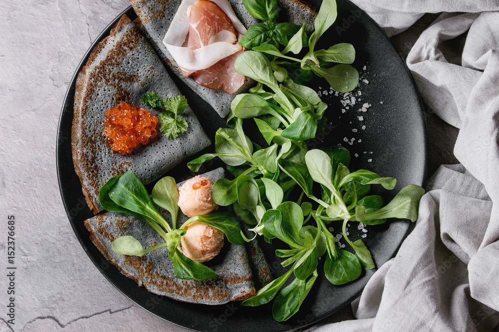 Black pancakes crepes with variety of salt filling red caviar, ham ...