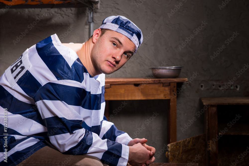 Young male prisoner wearing prison uniform looks at the camera while ...