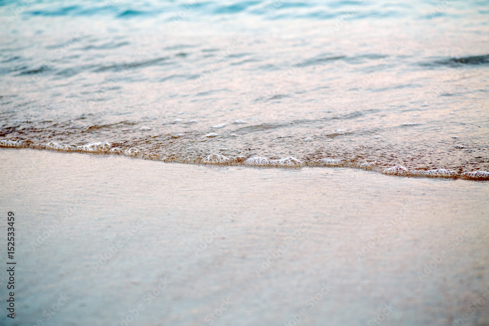 Closeup macro shot of sea ocean wave water with white foam, sandy beach ...