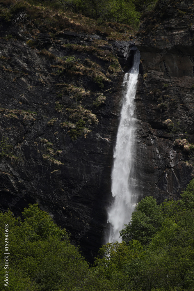 Water dripping down a tall mountain waterfall with lush vegetation ...