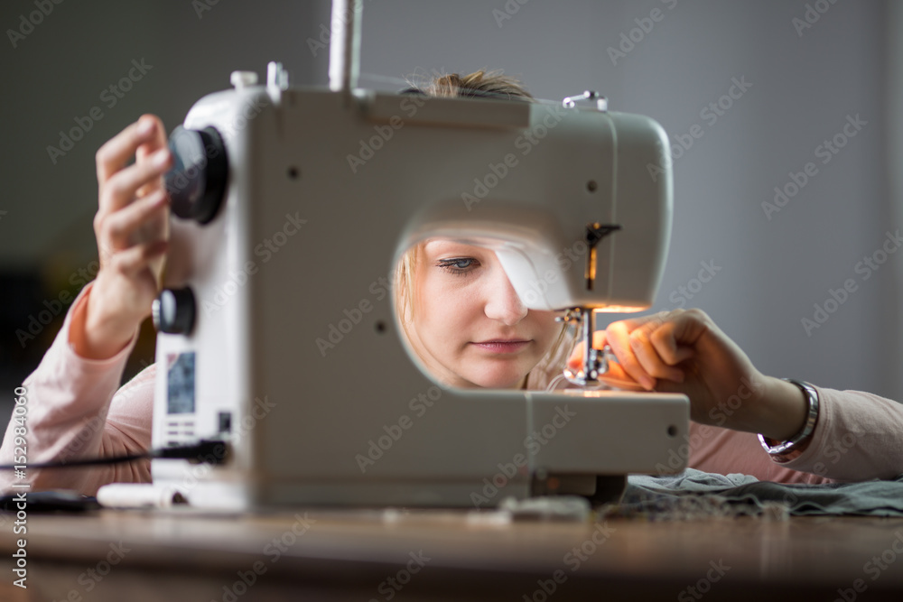 Beautiful young woman sewing clothes with sewing machine (color toned ...