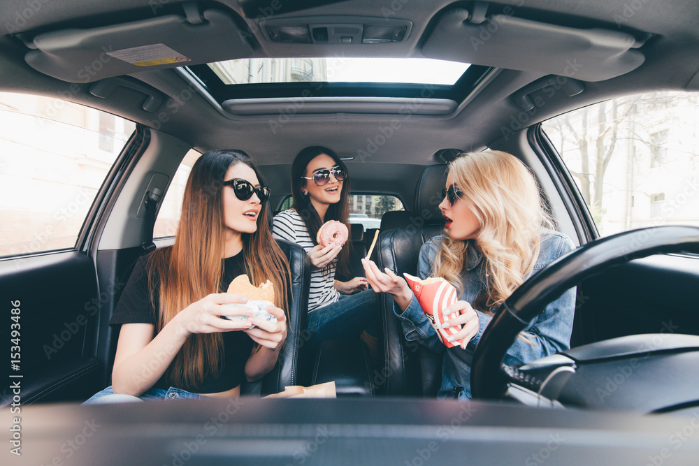 Enjoying their lunch in the car. Four beautiful young cheerful women ...