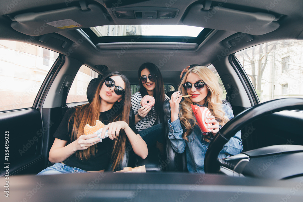 three girls driving in a car and having fun eating fast food in travel ...