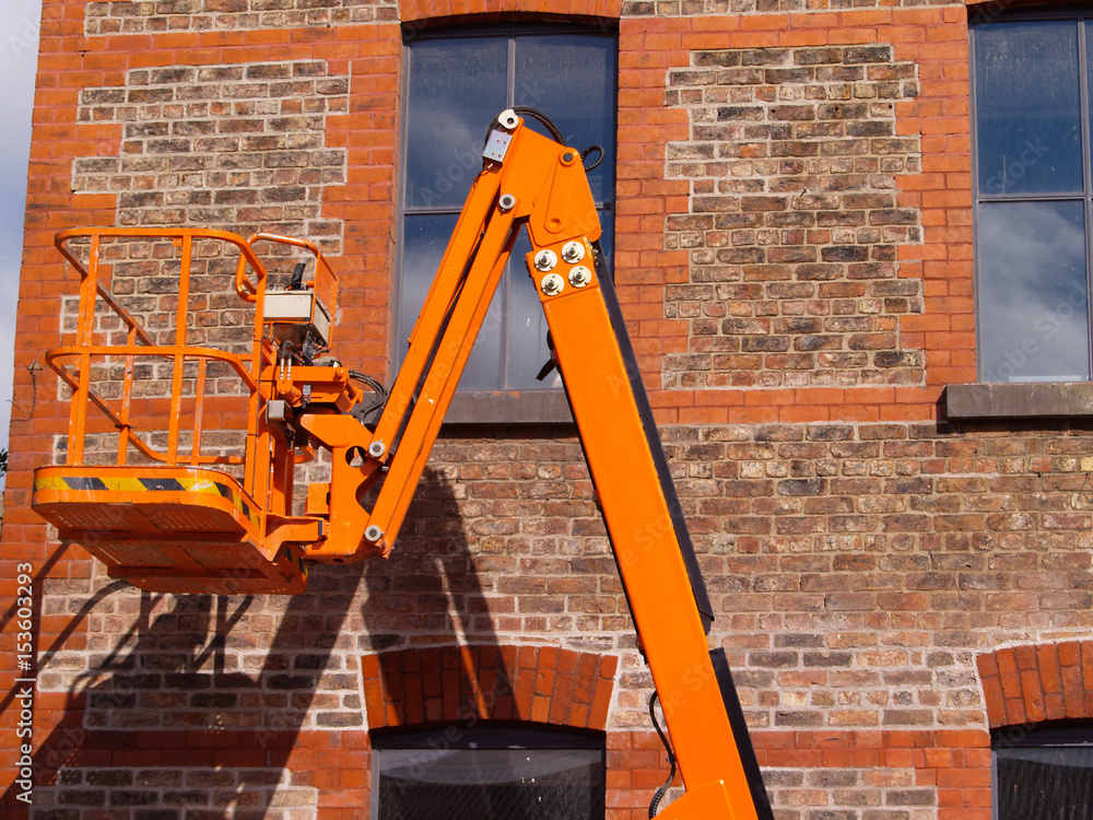 Orange coloured cherry picker next to old factory or warehouse building ...