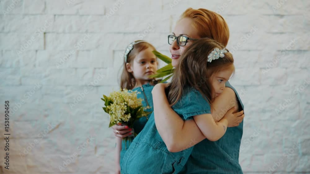 Mother and two little daughters are hugging each other with flowers and ...