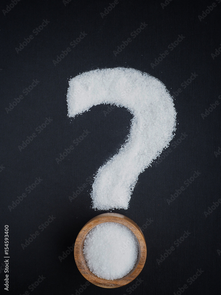 Salt spilled in the shape of question mark and wooden bowl on black ...