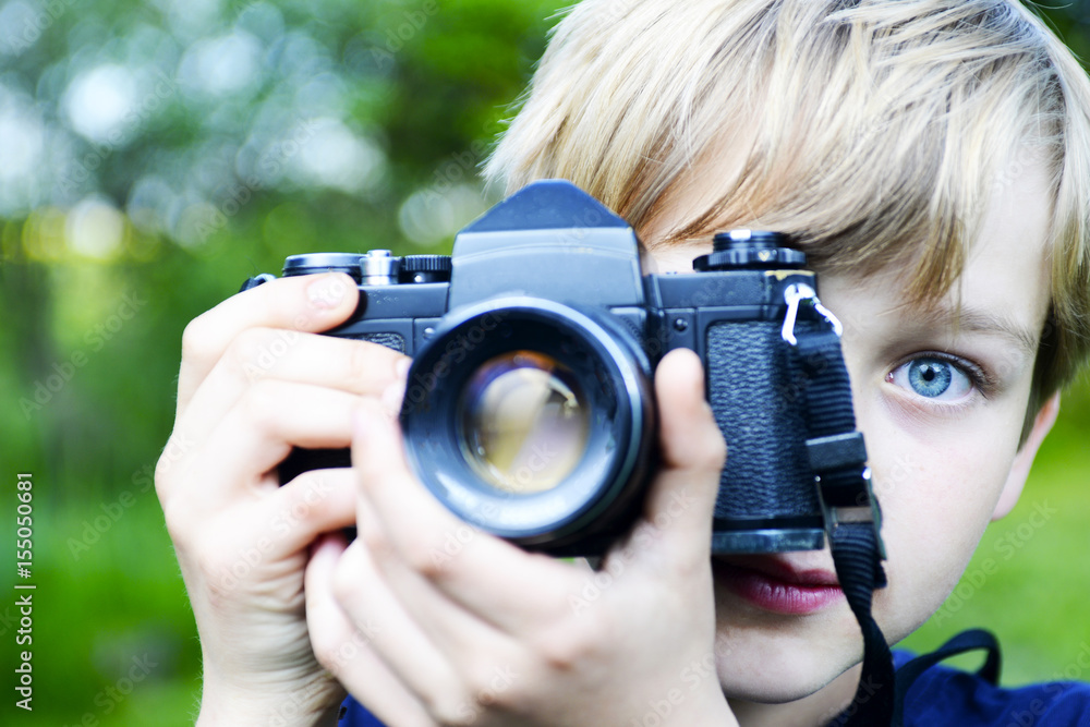 Little child blond boy with an old camera shooting outdoor. Kid taking ...
