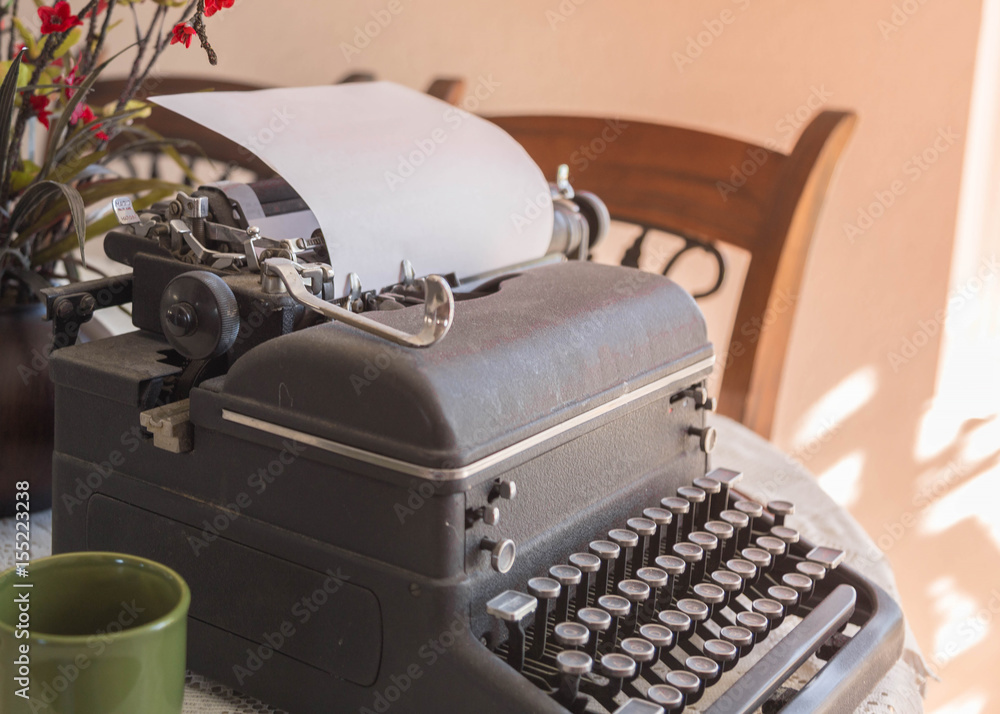 Old black vintage typewriter sitting on table next to red flower ...