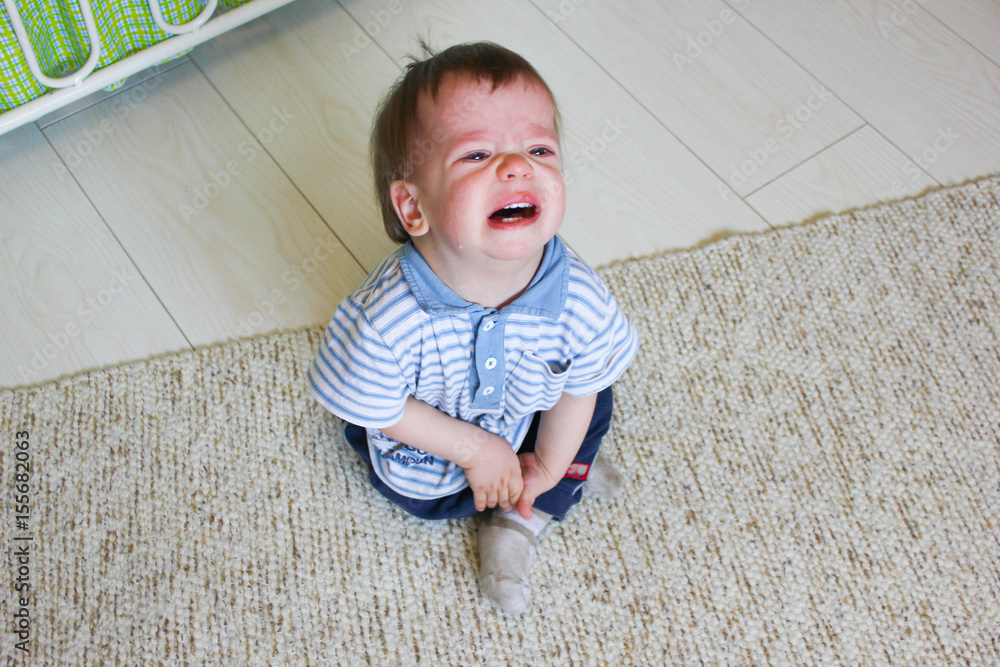 Little boy sitting on the floor, he's upset and crying. The child is ...