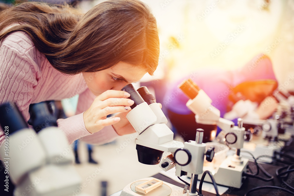 The student girl looks through a microscope in an equipped classroom ...