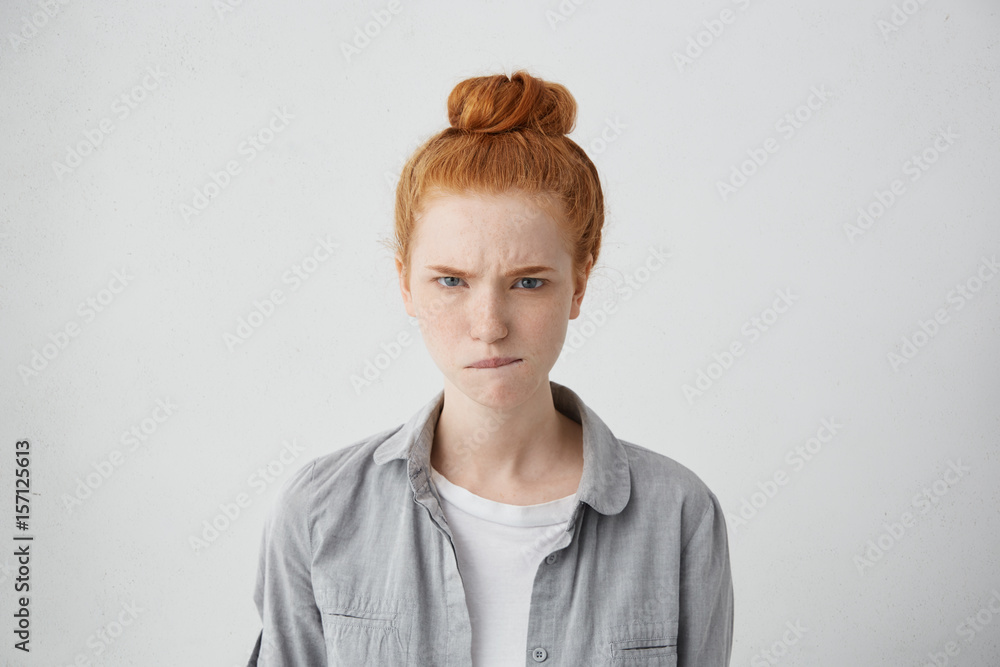 Portrait of angry frowning teenager having ginger bun biting her lip ...