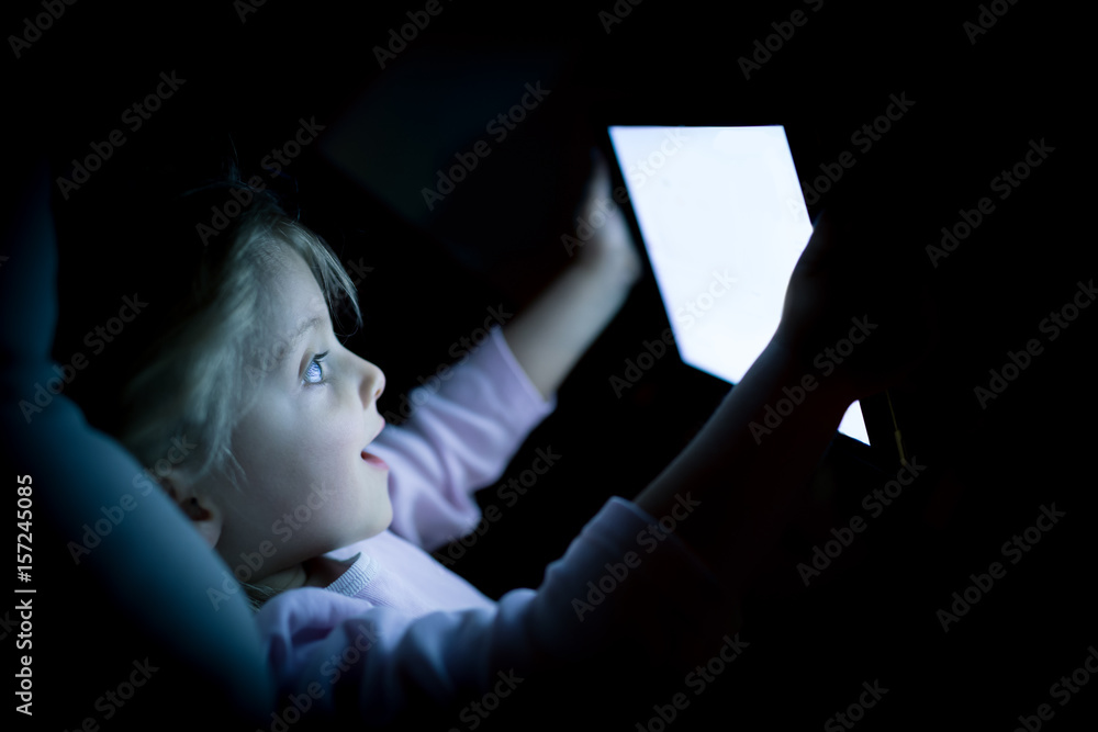 little child girl using tablet technology in bed by night at home ...