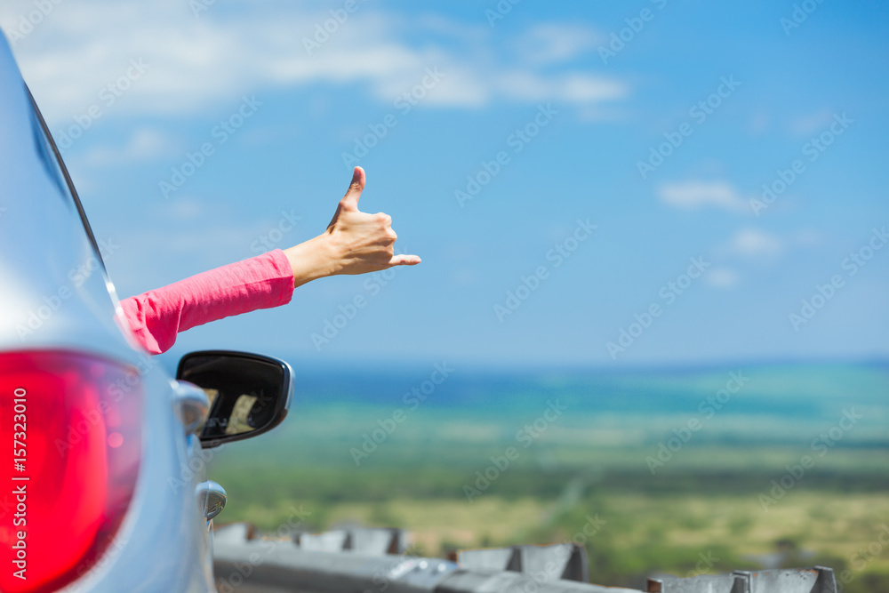 Road trip! Happy woman traveler making hang loose hand sign out of car ...