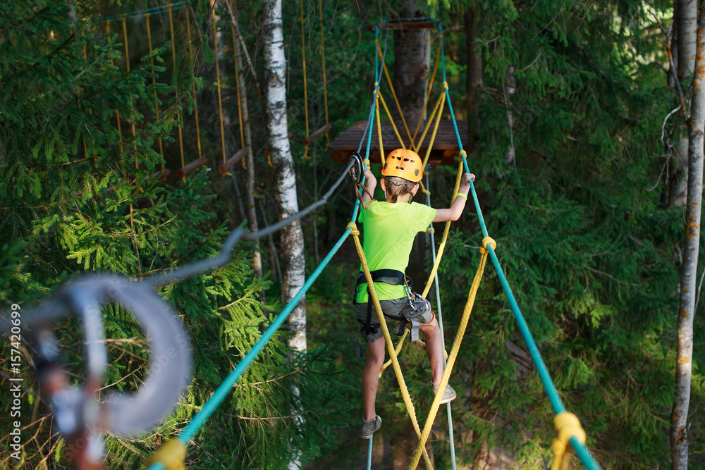 boy climbs in a high wire park above the ground. ziplining. boy on the ...