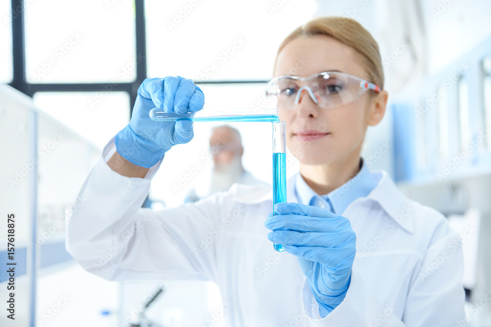 Smiling chemist in white coat holding test tubes with reagents and ...