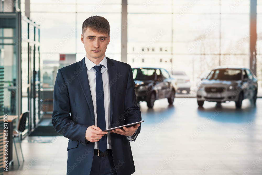 Serious but affable car salesman in a business man suit car dealership ...