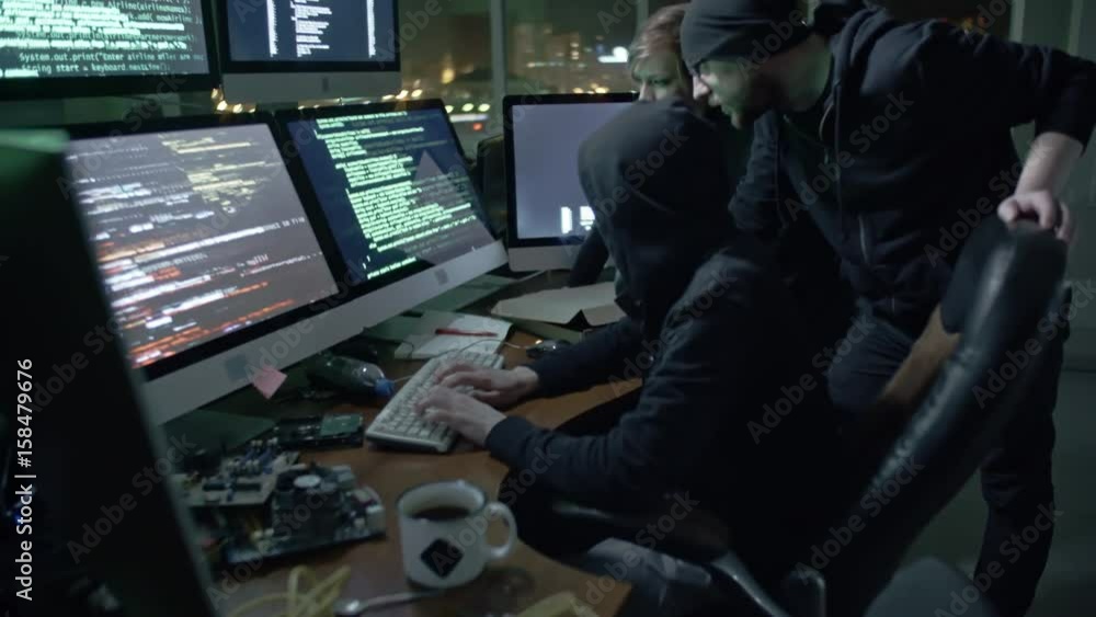 Tilt up of team of hackers typing programming code on computer monitors in office at night Stock ...